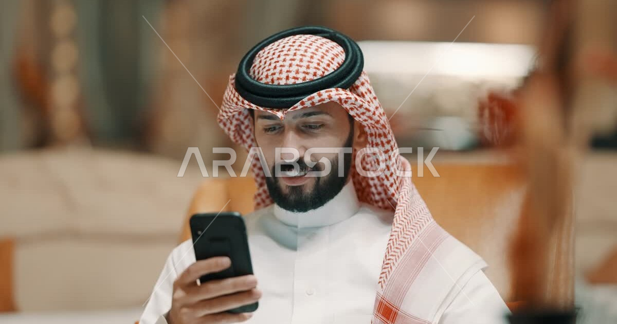 A Saudi Arabian Gulf man sitting on the sofa, using a mobile phone ...