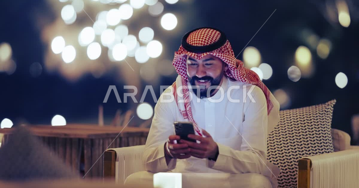 A Saudi Arabian Gulf man sitting on the sofa, using a mobile phone ...