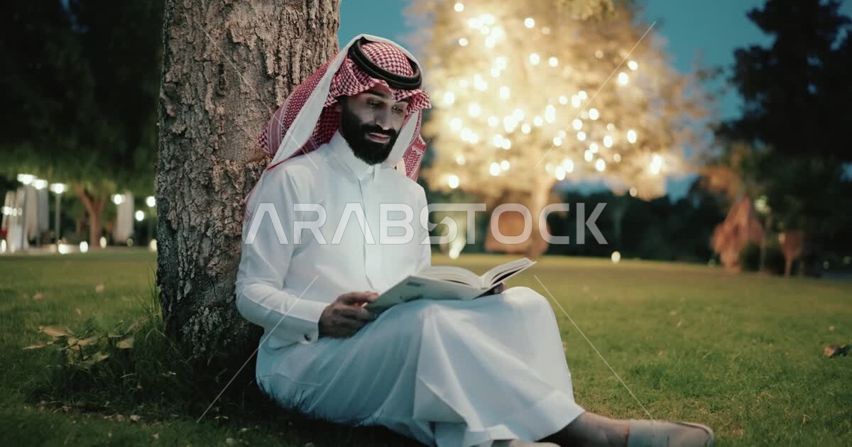 A Saudi Arabian Gulf man dressed in traditional Saudi dress reading a ...