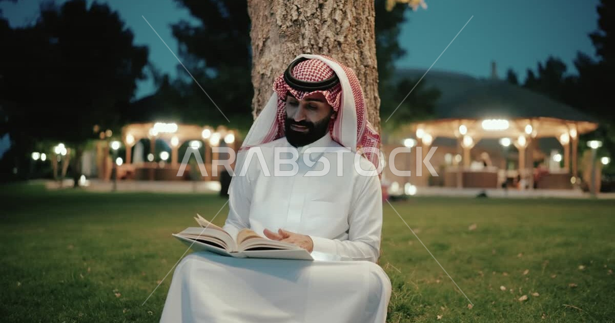 A Saudi Arabian Gulf man dressed in traditional Saudi dress reading a ...