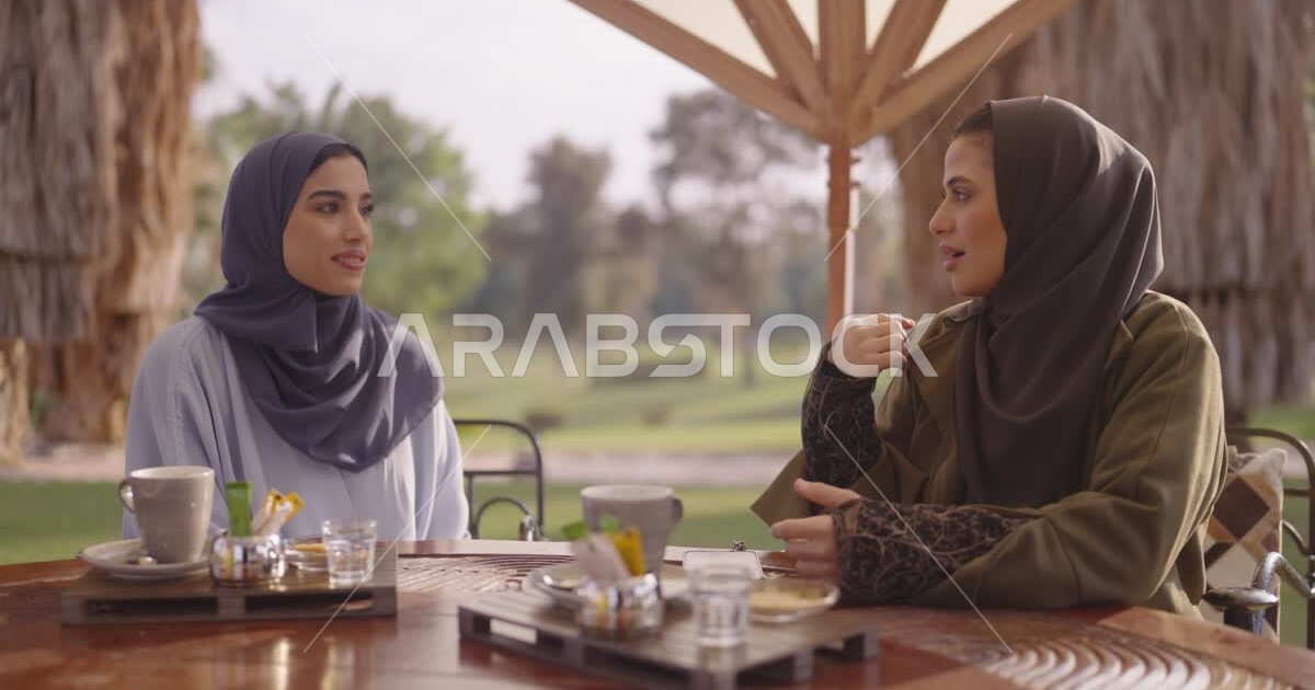 Two Saudi Arab Gulf women sitting in a public garden in the open air ...
