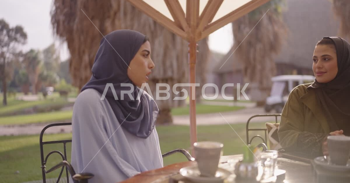 Two Saudi Arab Gulf women sitting in a public garden in the open air ...