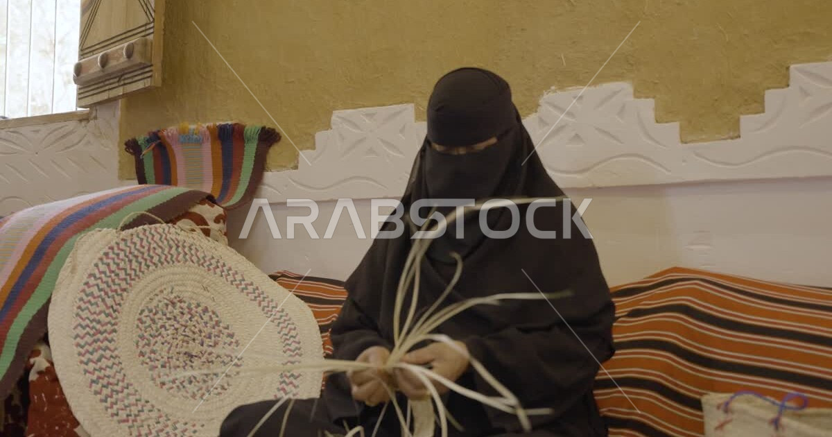 A Saudi Arab Gulf woman wearing a veil braids wicker palms, traditional ...