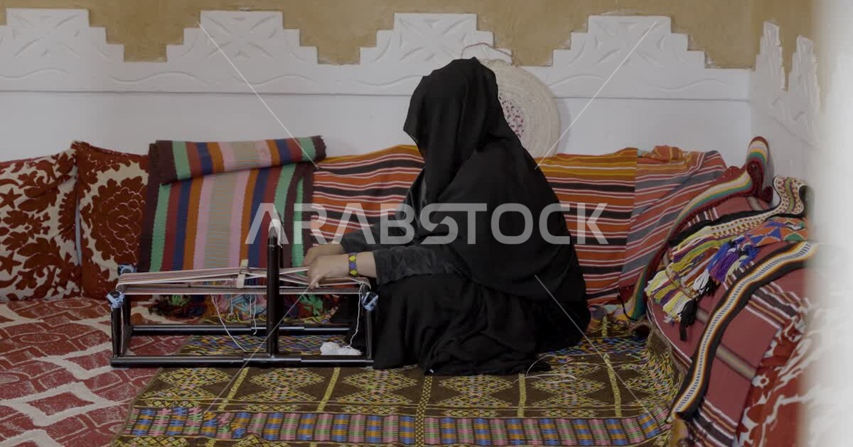 سيدة عربية خليجية سعودية منقبة تقوم بحياكة وغزل الانسجة والقماش، صناعات