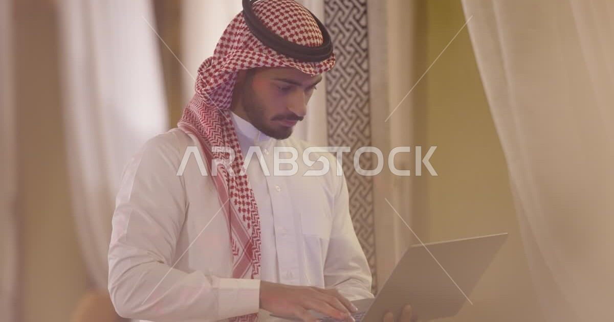 A Saudi Arabian Gulf man using a laptop, working remotely, using modern ...