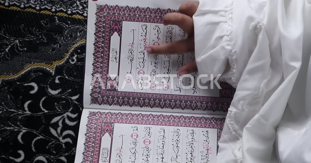 Close-up of a girl holding the Holy Qur’an in her hand, reading the ...