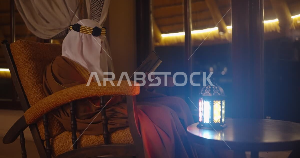 A Saudi Arabian Gulf man sitting on a chair, holding the Holy Qur’an ...