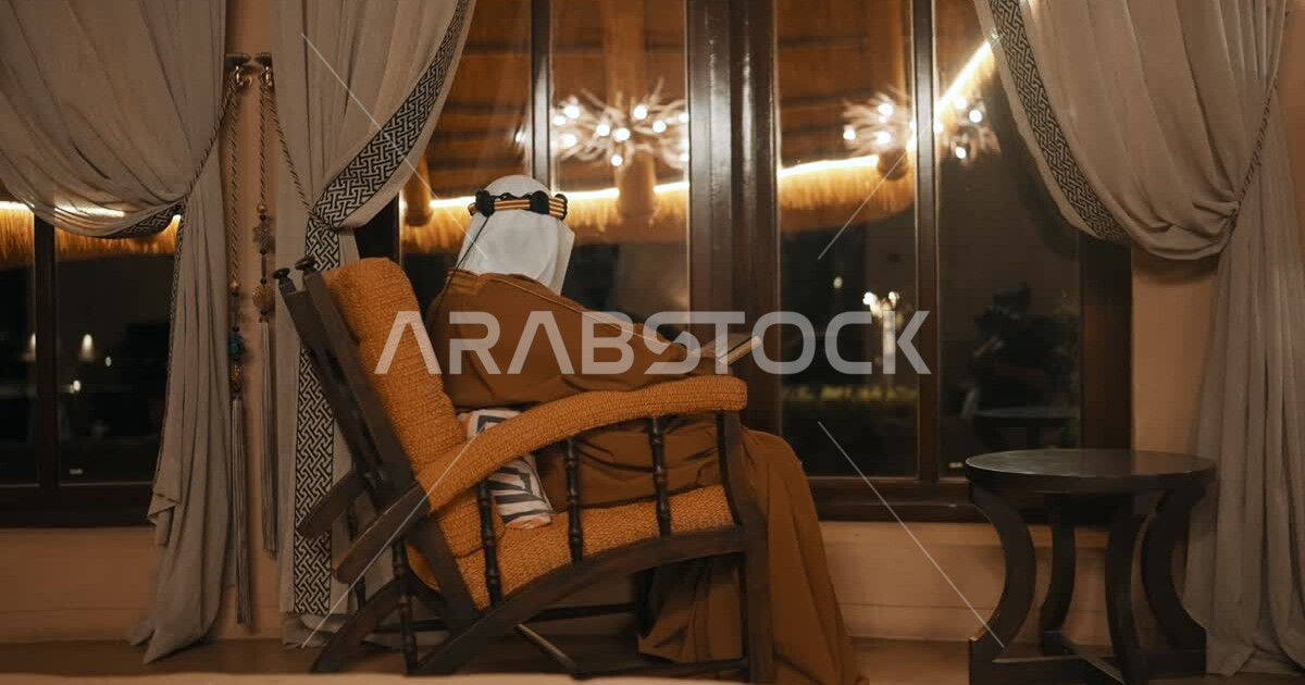 A Saudi Arabian Gulf man sitting on a chair, holding the Holy Qur’an ...