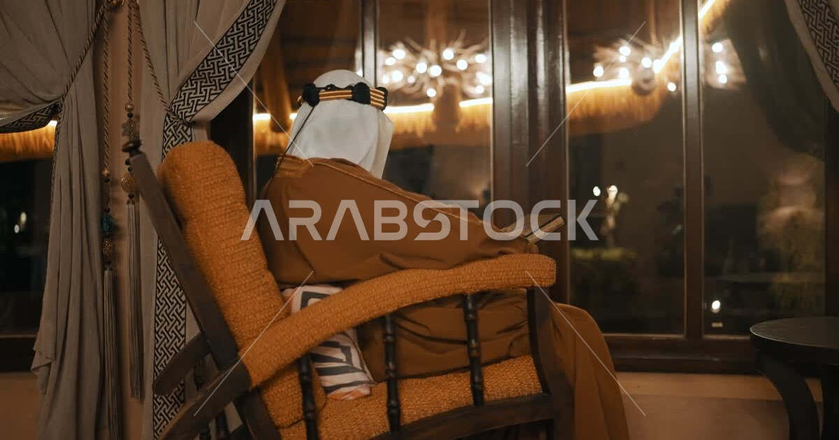 A Saudi Arabian Gulf man sitting on a chair, holding the Holy Qur’an ...