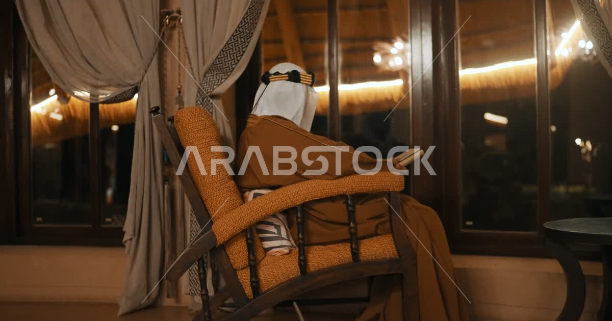 A Saudi Arabian Gulf man sitting on a chair, holding the Holy Qur’an ...