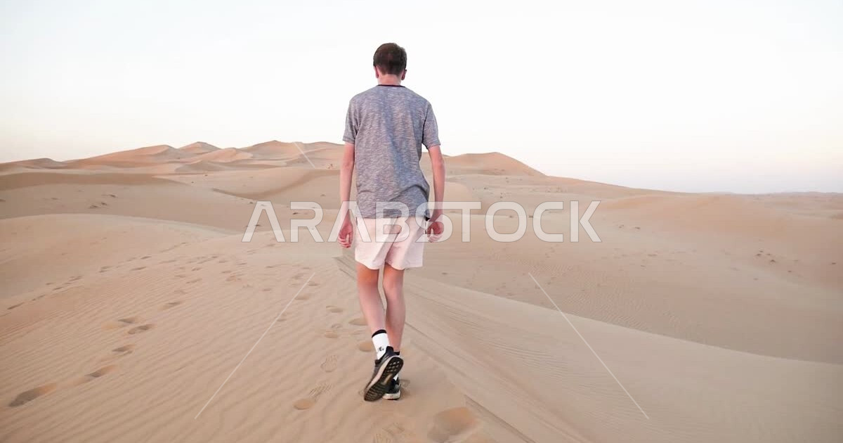 Back view of a young man wandering in desert areas, sandy hills, sand ...