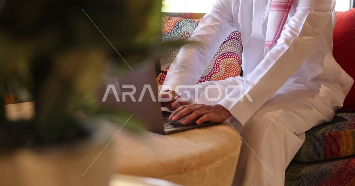 Close-up of a Saudi Arabian Gulf man sitting on the sofa, using a ...