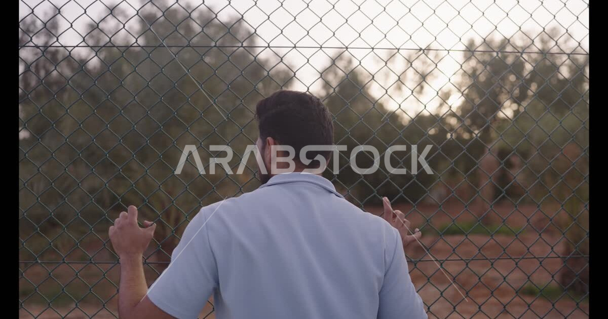 Views from behind of a Saudi Arabian Gulf man on an iron mesh fence ...