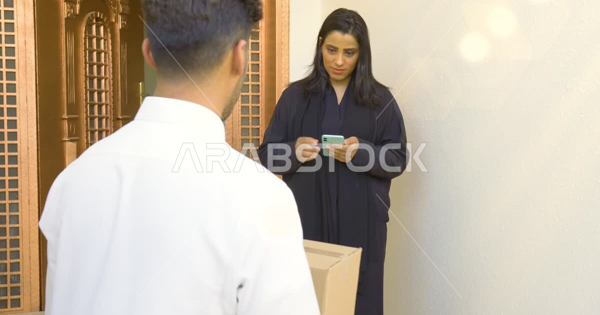 A Saudi Arabian Gulf woman using a mobile phone, signing the receipt of ...