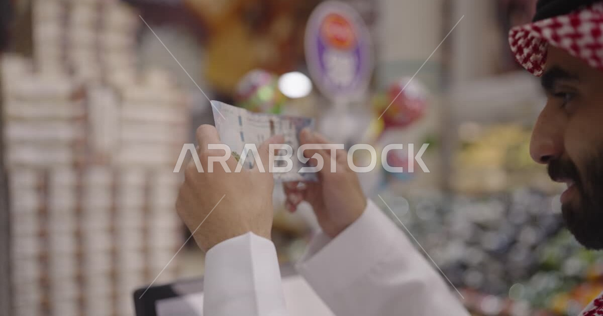 A Saudi Arabian Gulf man in a food store holding a banknote, paper ...