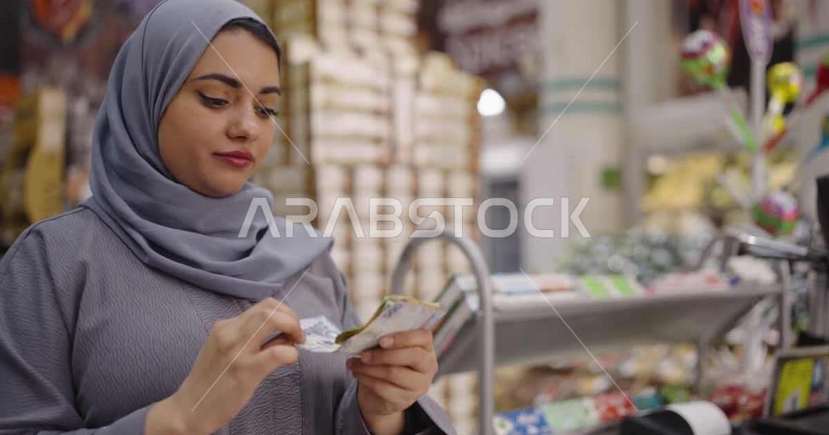 A Saudi Arab woman inside a food store carrying banknotes, commodities ...